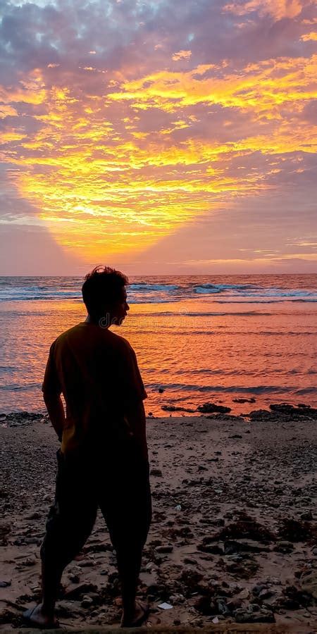 Un Hombre Parado En La Playa Con Un Fondo De Puesta De Sol Que Emite