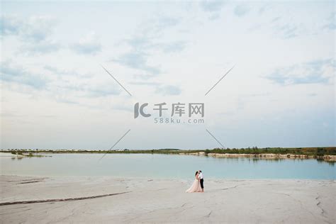 一对年轻夫妇一个穿黑色马裤的男人和一个穿粉红色连衣裙的女孩正沿着白色沙滩散步高清摄影大图 千库网