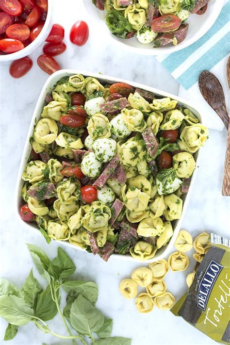 Two Bowls Filled With Pasta Salad Next To Tomatoes And Spinach On A
