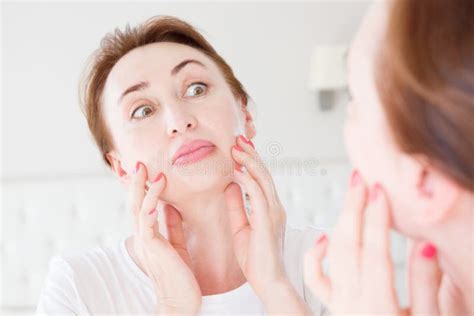 Mujer De La Edad Media Que Mira En Espejo En Cara De La Arruga En La
