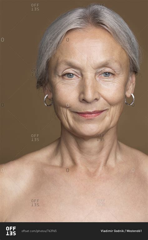 Portrait Of Naked Senior Woman With Grey Hair In Front Of Brown