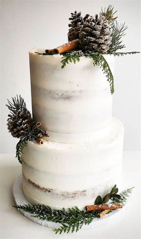 A Three Tiered White Cake With Pine Cones On Top And Evergreen Sprigs