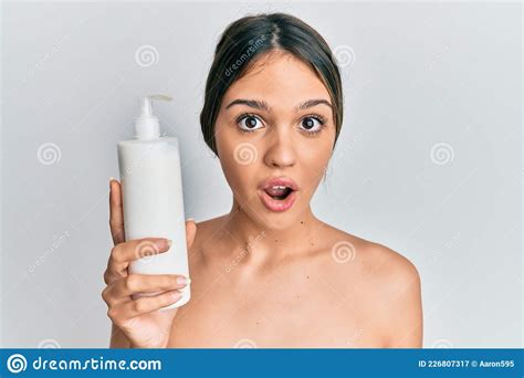 Young Brunette Woman Holding Cosmetic Moisturizer Facial Cream Scared And Amazed With Open Mouth