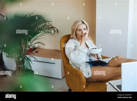 Blonde Caucasian Woman Sitting In Armchair And Looking Away Holding A