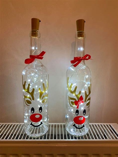 Two Glass Bottles Decorated With Lights And Reindeer Heads Are Sitting