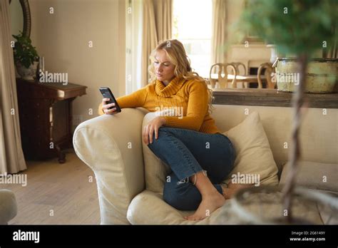 Caucasian Woman Sitting On Couch Relaxing In Luxury Living Room Using