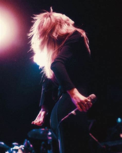 A Woman Standing In Front Of A Drum Set On Stage With Her Hands Behind