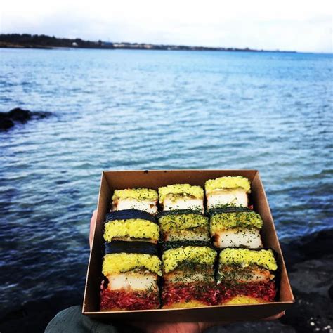 Someone Holding Up A Box Of Sushi By The Water