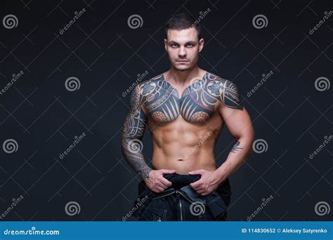 The Man With A Muscular Naked Torso With Tattoos On The Dark Background