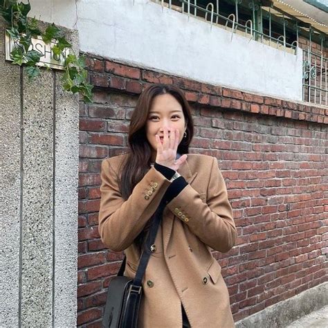 A Woman Standing In Front Of A Brick Wall Holding Her Hand Up To Her Mouth