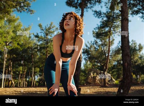 Young Redhead Woman Wearing Sportive Clothes Standing On City Park Outdoors Standing Bent Over