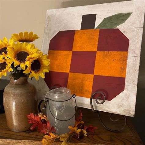 Sunflowers Are In A Vase Next To An Apple Shaped Painting On A Table