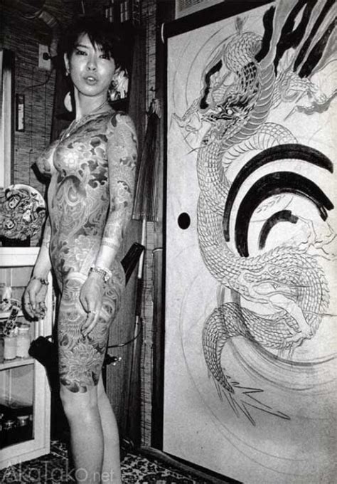 A Woman With Tattoos Standing In Front Of A Dragon And Snake Tattoo On
