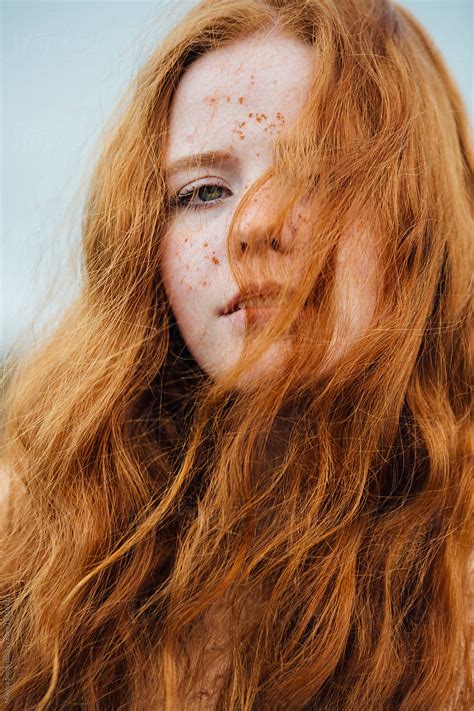 Close Up Portrait Of A Young Woman With Ginger Hair And Freckles With Her Hair Blowing Over Her