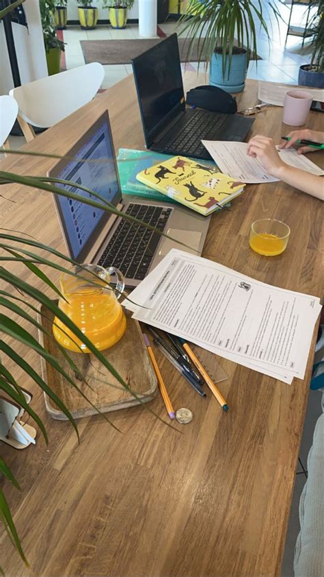 A Person Sitting At A Desk With Two Laptops And Papers On The Table