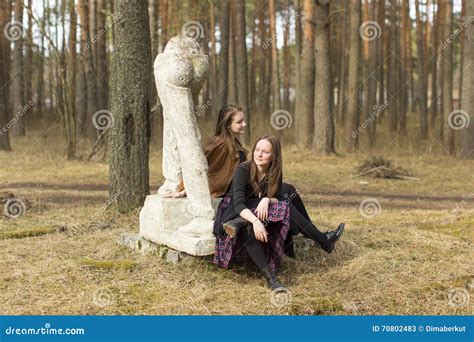 Filles De Jeune Adolescent S Asseyant Aux Vieilles Sculptures En Parc