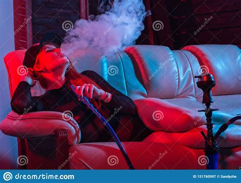 Redhead Woman In Black Bodysuit Sitting On A Sofa And Smokes Hookah Girl Blows Out Big Smoke