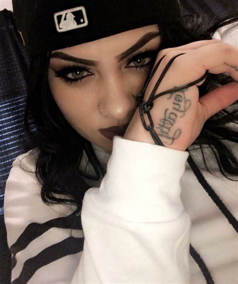A Woman With Tattoos On Her Arm And Wearing A Baseball Cap Is Posing