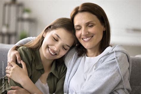 Happy Peaceful Mom And Pretty Teenage Kid Girl Sitting Close On Home
