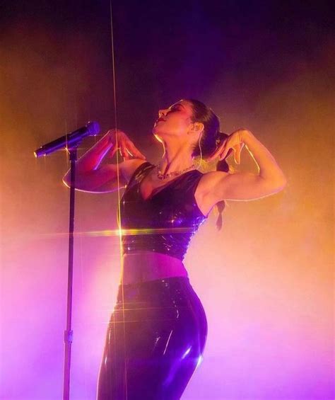 The Woman Is Singing On Stage With Her Hands Behind Her Back As She