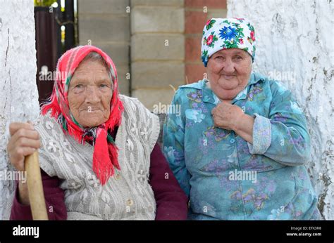 Portrait Of Two Old Russian Women Sitting Near House Between Two An Old