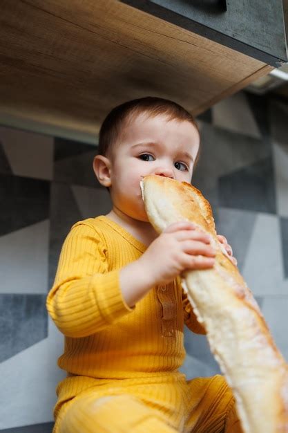 Un niño pequeño de un año está sentado en la cocina y comiendo un pan