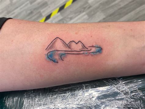 A Tattoo On The Arm Of A Person With Mountains In The Background And