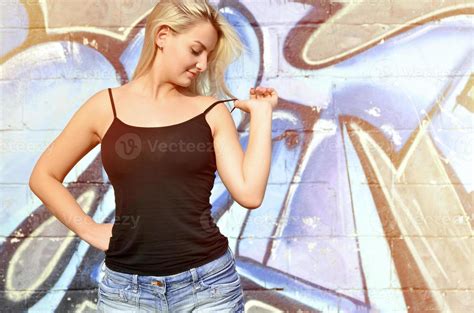 Sexy Caucasian Blonde Girl In Denim Shorts And Black Tank Top Posing Against Graffiti Wall In
