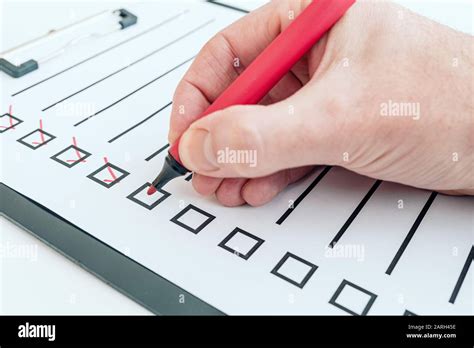 Close Up Of Hand Holding Red Pen Ticking Off Checklist Or To Do List On