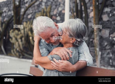 Middle Age Woman Sitting On Bench Of Park With Old Man Hugging Her From