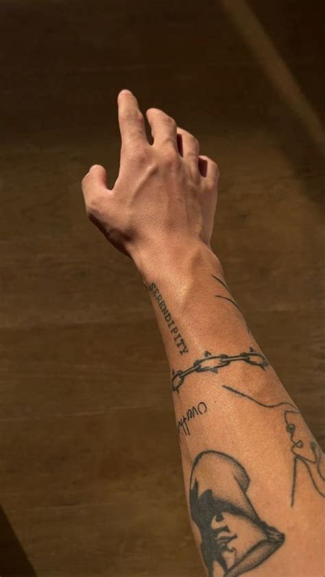 A Person With Tattoos On Their Arm Holding A Cell Phone Up To The Sky