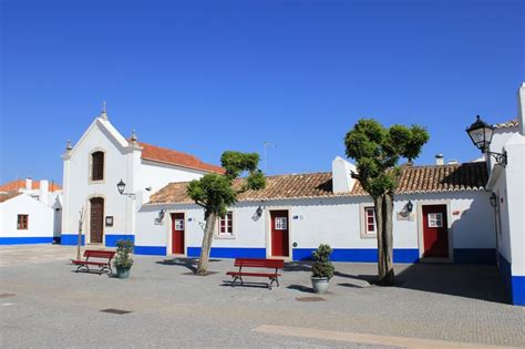 Two Red And Blue Benches In Front Of A White Building With Trees On