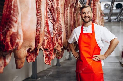 Premium Photo Young Butcher At The Meat Factory Standing By The Hanging Meat