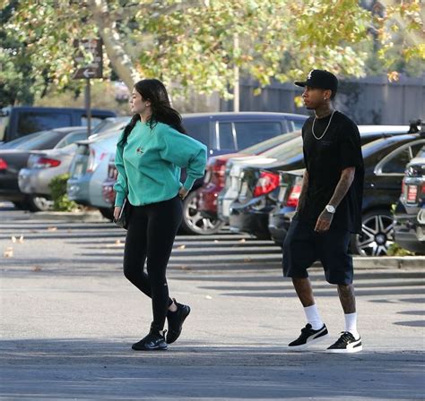 A Man And Woman Walking Down The Street In Front Of Parked Cars
