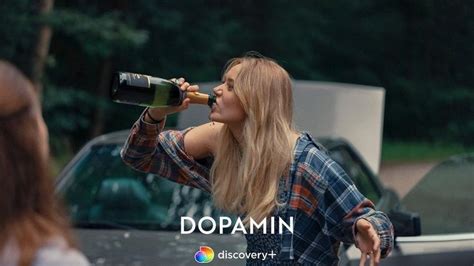 A Woman Drinking From A Bottle While Standing In Front Of A Car With