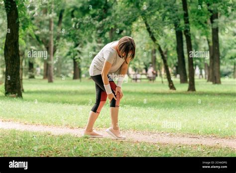 Female Jogger With Painful Knee Injury During Park Jogging Activity