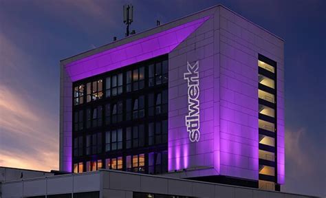 A Tall Building With A Purple Light On It S Side And Windows Lit Up At