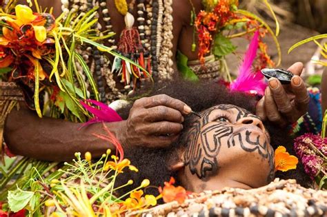 A Man Is Getting His Face Painted With Flowers And Feathers As He Lays