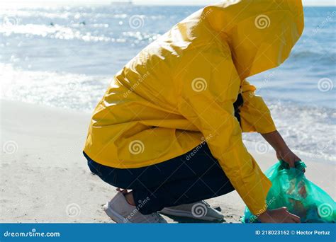 Woman In Raincoat Picking Up Plastic Bent Over On Beach Stock Photo