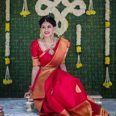 A Woman In A Red And Gold Sari Sitting On A White Table With Flowers