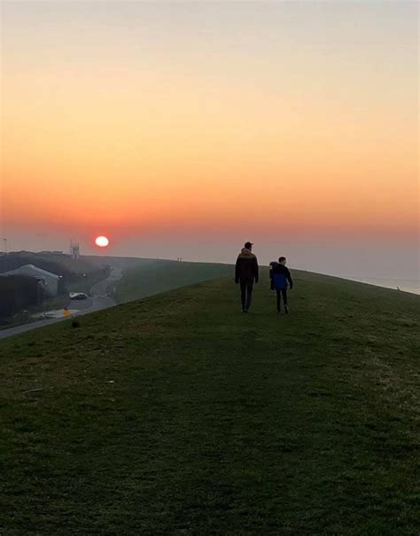Two People Walking Down A Hill At Sunset With The Sun Setting In The