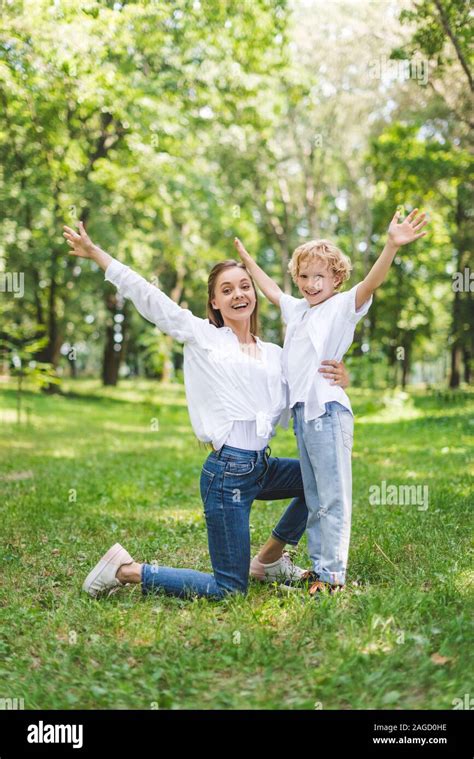 Beautiful Smiling Mom And Son With Raised Hands In Park Looking At