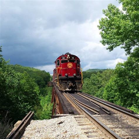 A Red Train Traveling Over A Bridge Next To Lush Green Trees On A