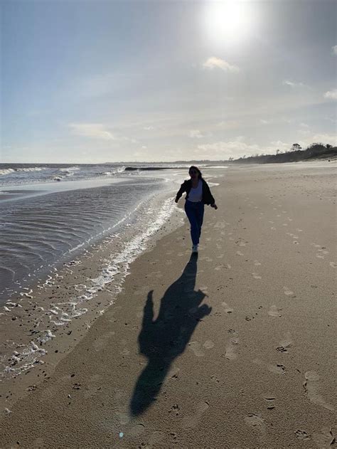 A Person Is Walking Along The Beach With Their Shadow On The Sand As