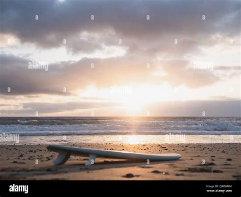 Surfboard Lying On The Beach And The Sunrise In A Cloudy Sky Stock