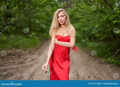 Beautiful Young Long Haired Blonde In A Red Dress Posing On The Road In A Summer Park With A