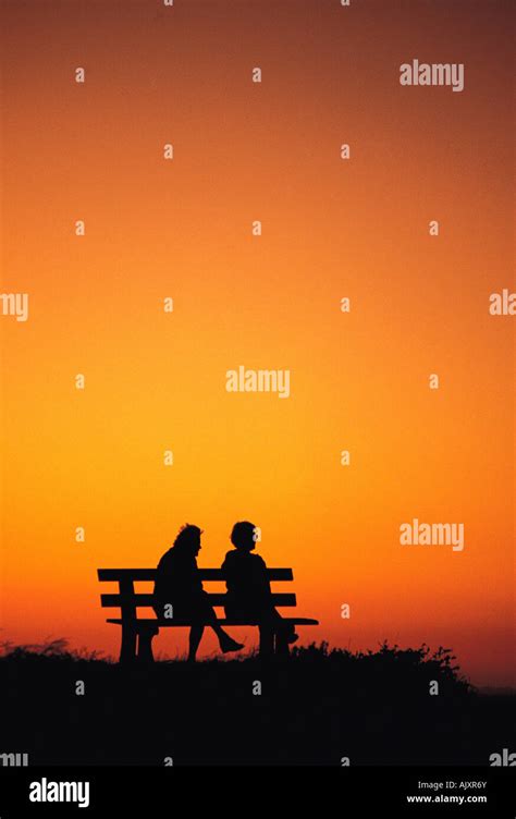 Silhouette Of Two Old Women Sitting On Park Bench At Sunset Stock Photo