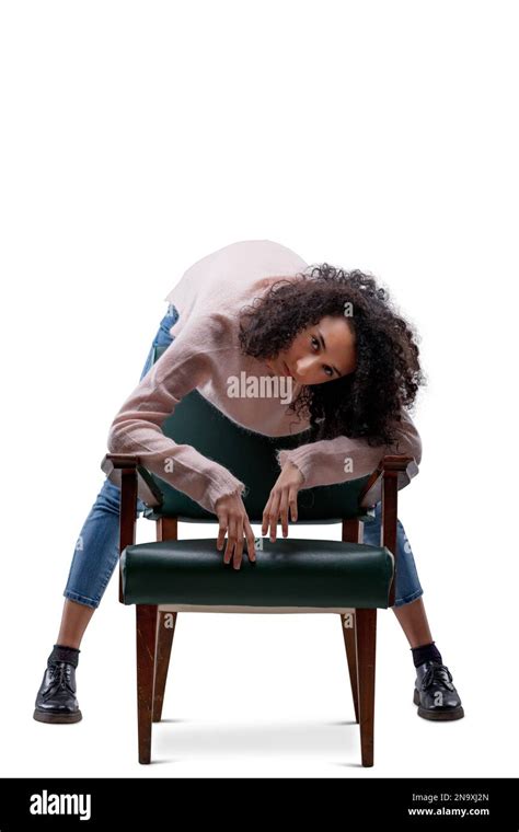 Young Curly Haired Woman Hunched Over A Chair In Front Of Her Holding Her Long Legs Straight And