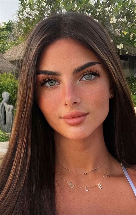 A Woman With Long Brown Hair And Blue Eyes Wearing A White Top Is
