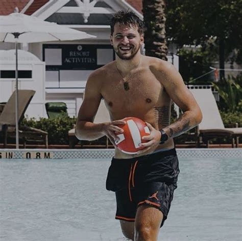 A Shirtless Man Is Holding A Ball In The Water Near A Resort Swimming Pool